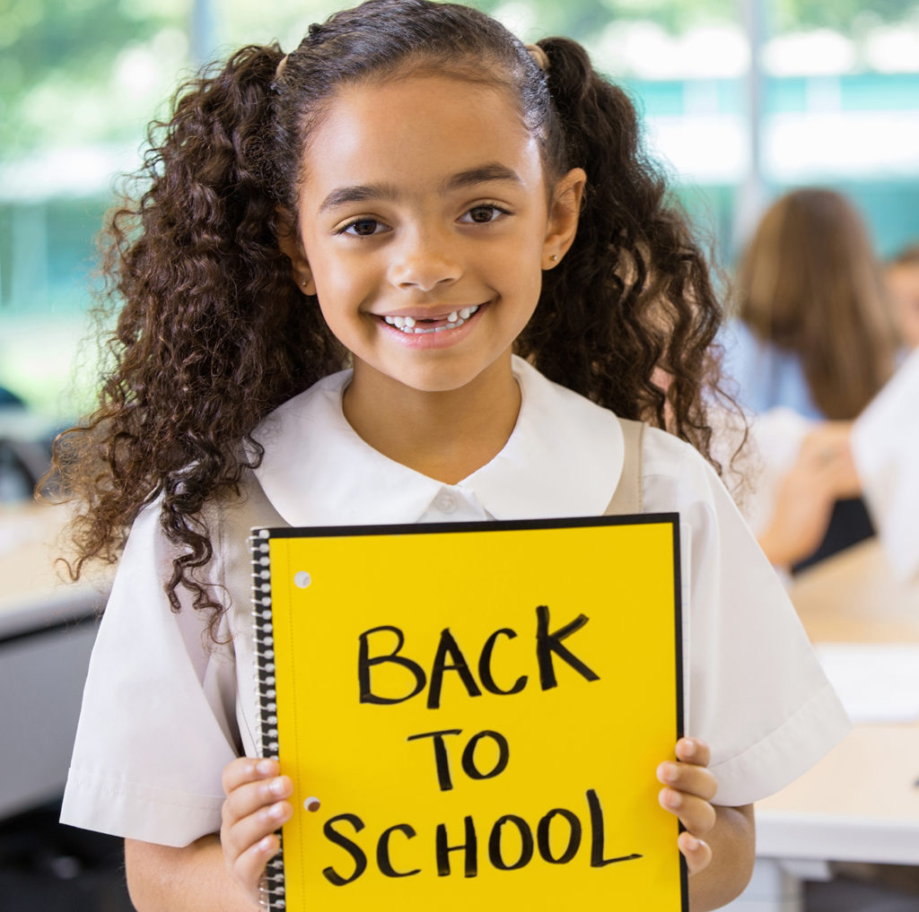 Elementary student holding "back to school" sign while wearing uniform - Eckerd Connects